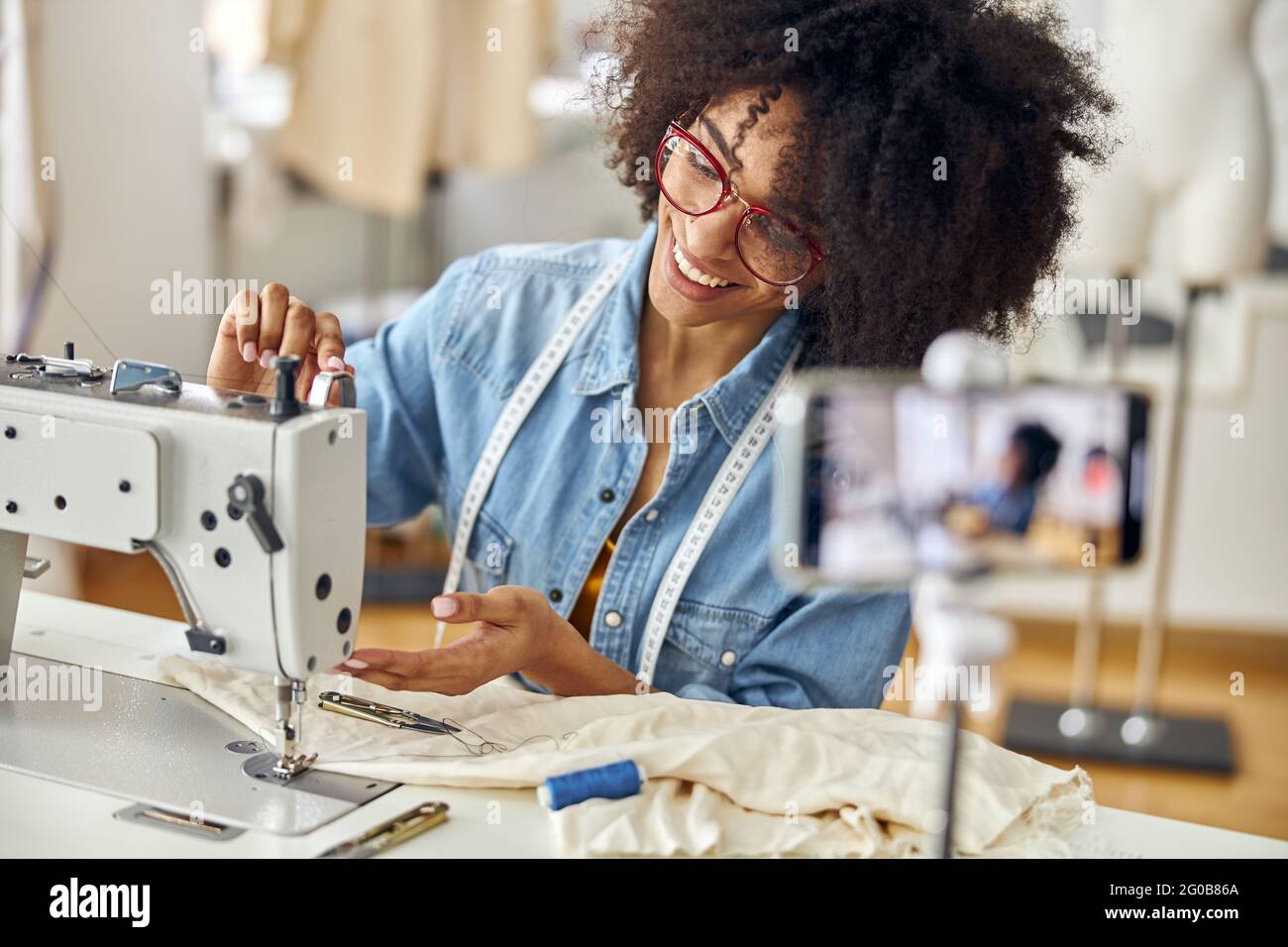 Smiling African-American seamstress adjusts sewing machine shooting new ...
