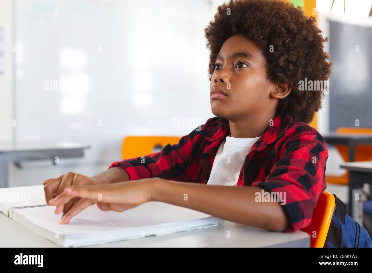 Blind african american schoolboy sitting at desk in classroom reading ...