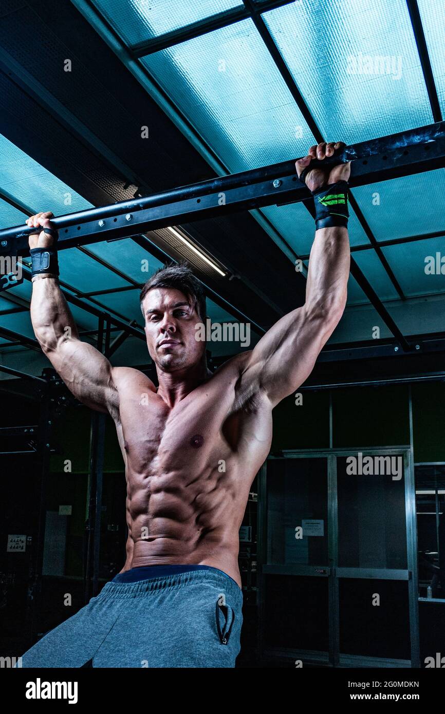 Vertical shot of a fit male bodybuilder hanging from a bar at the gym ...