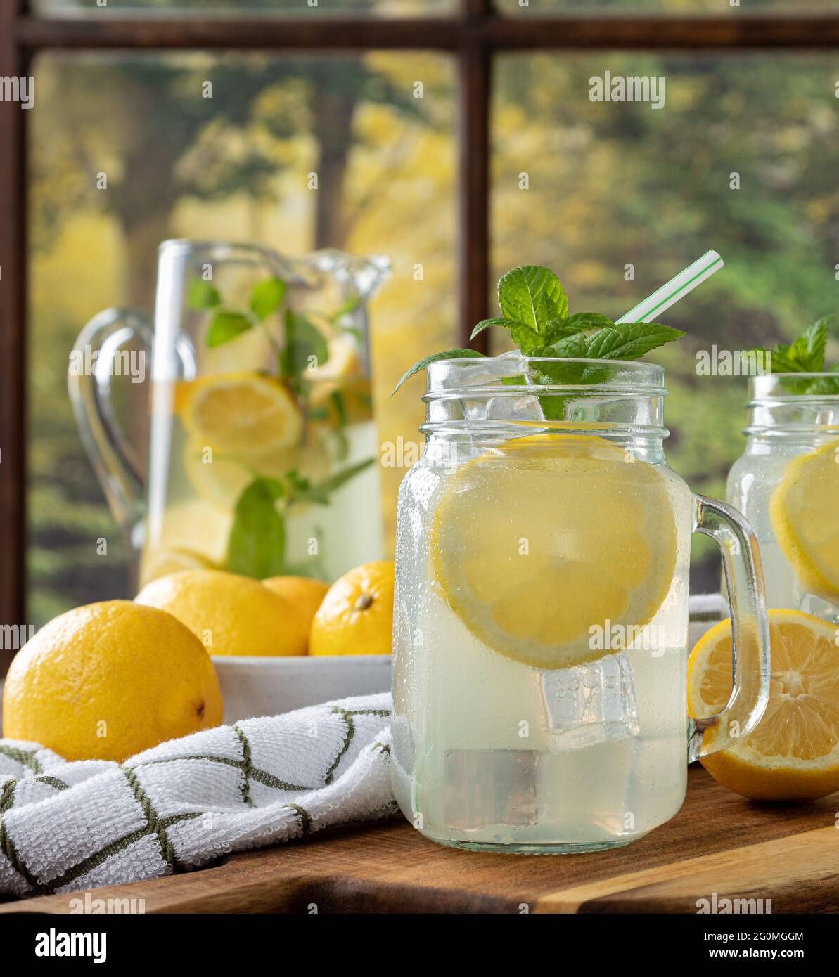 Glass of lemonade with lemon and mint by a window with rural background ...