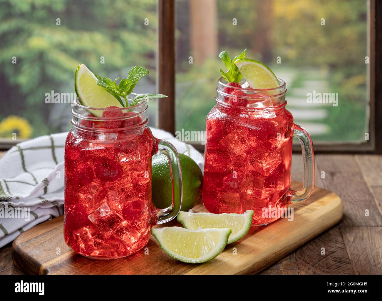 Two glasses of cranberry juice with raspberries and lime by a window ...