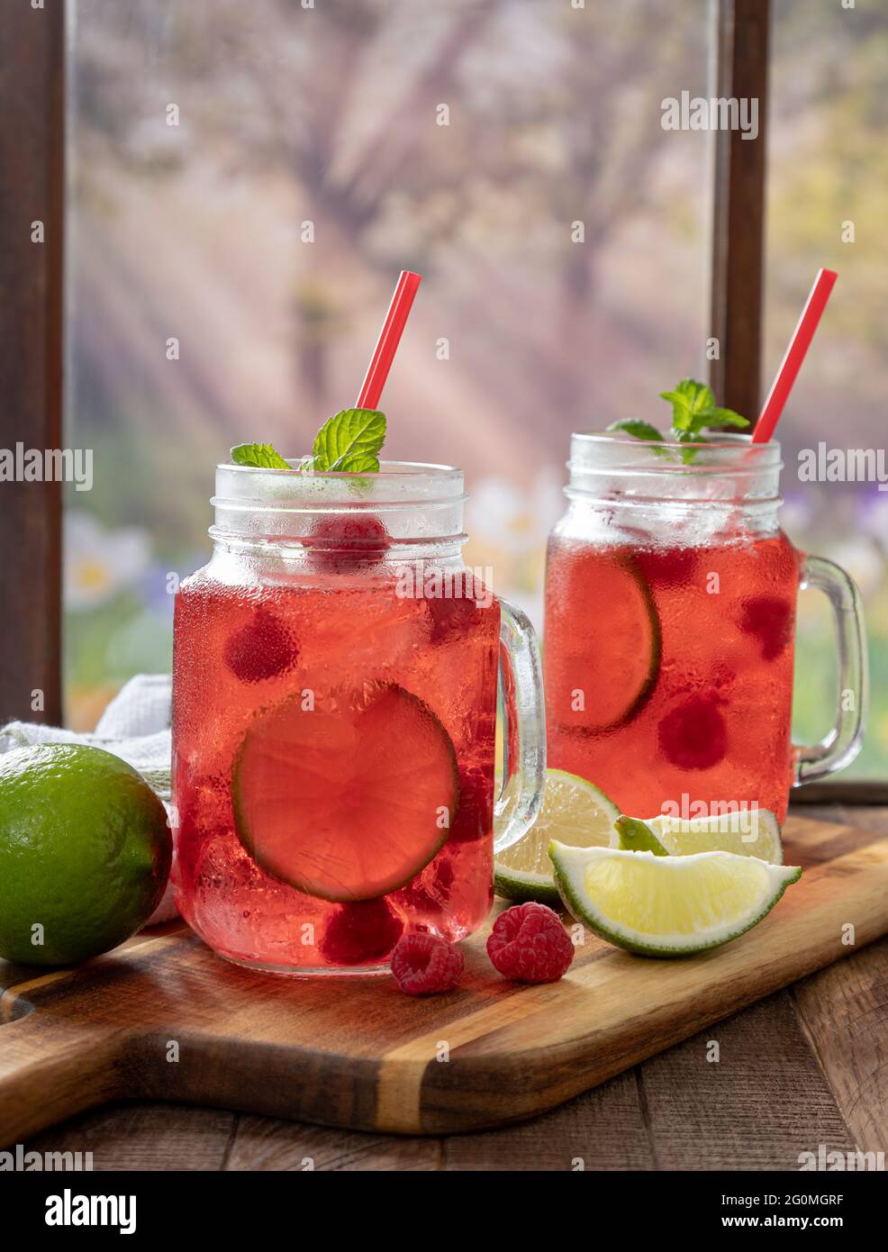 Two glasses of cranberry juice with raspberries and lime by a window ...