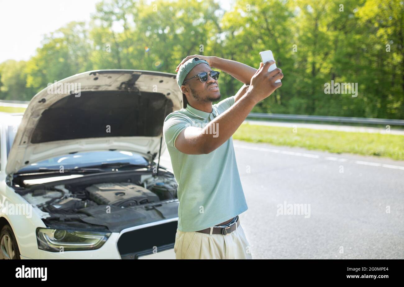 Upset black guy standing near broken car with open hood, having problem ...