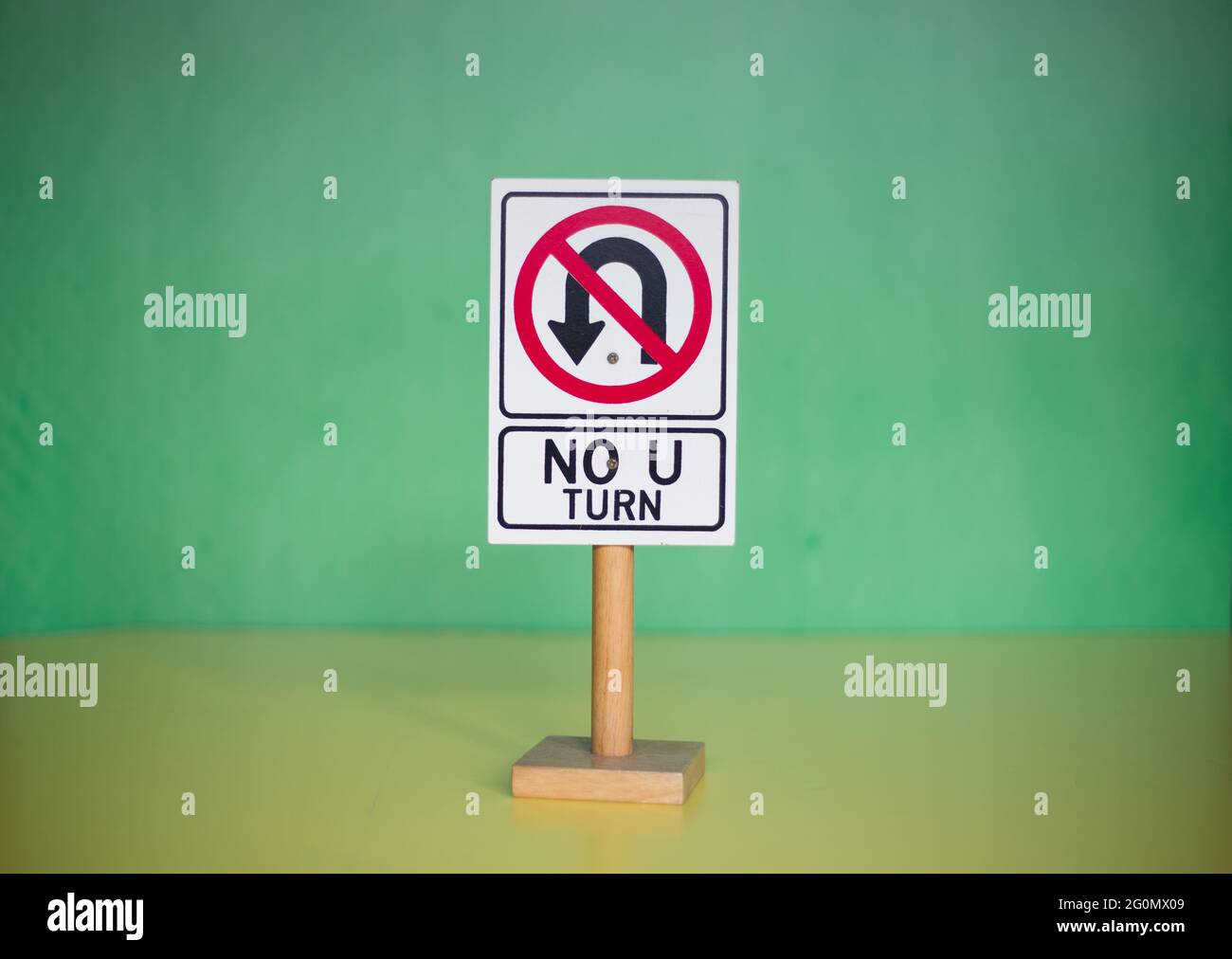 Closeup of a toy "NO U TURN" sign on a wooden stand against a green ...