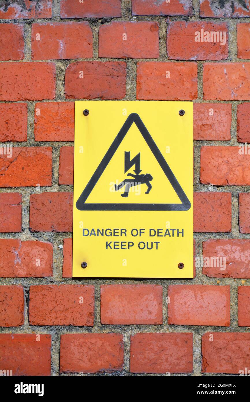 Bright yellow warning sign, danger of death, on a brick wall outside an ...