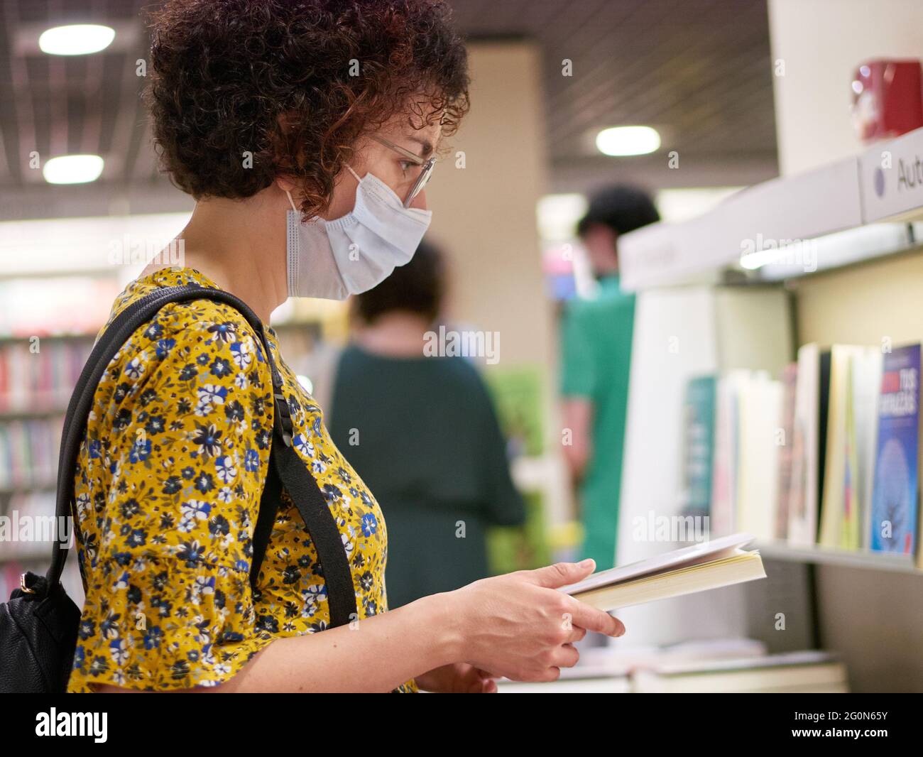 A woman looking at books in a bookstore wears a face mask that protects ...