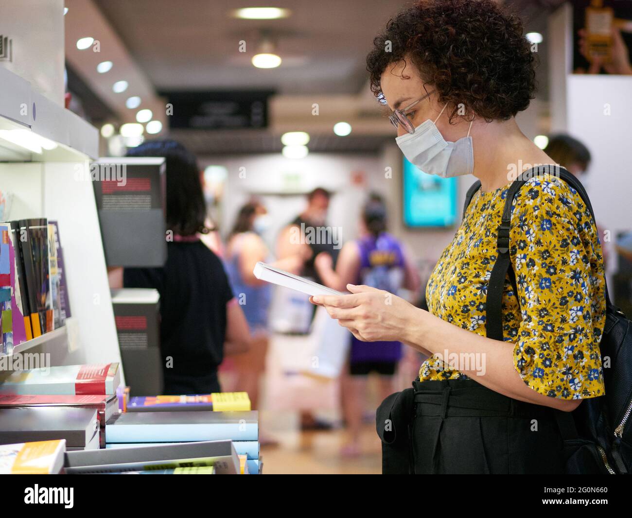 A woman looking at books in a bookstore wears a face mask that protects ...