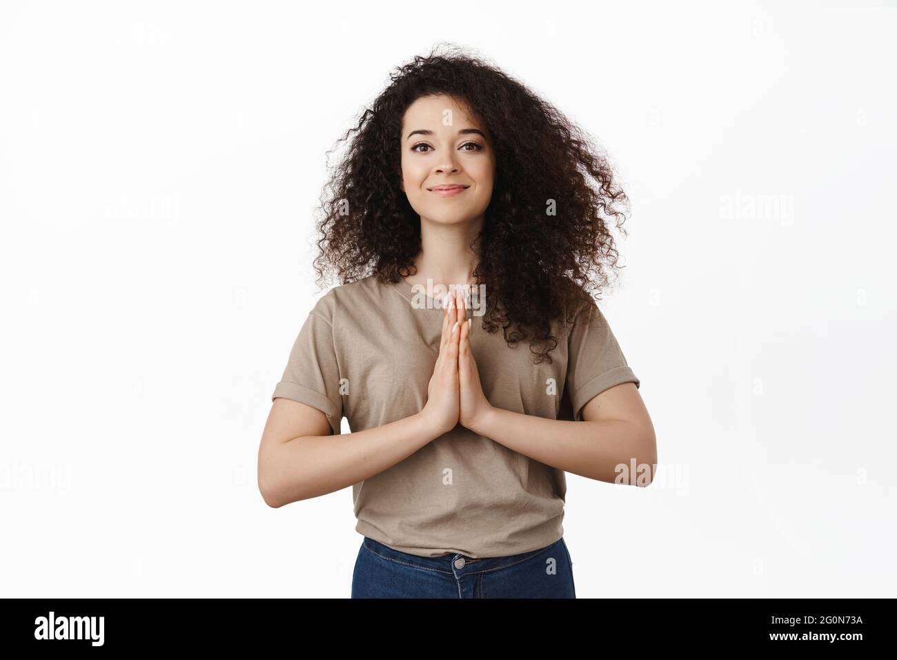 Namaste. Smiling relaxed brunette woman holding palms together, looking ...