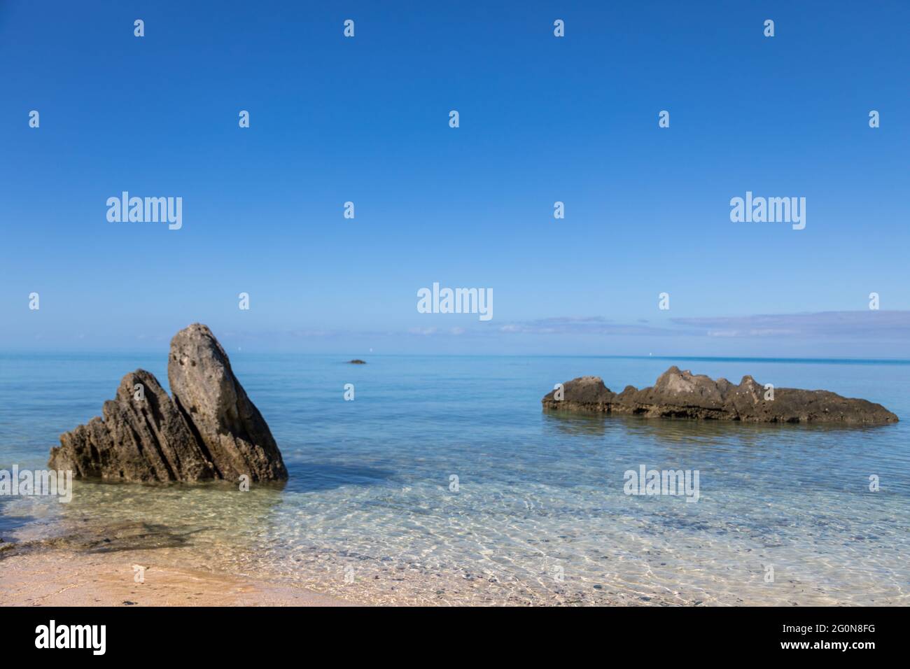 Large Rocky outcrop on a quiet beach, calm blue sky and ocean scene ...