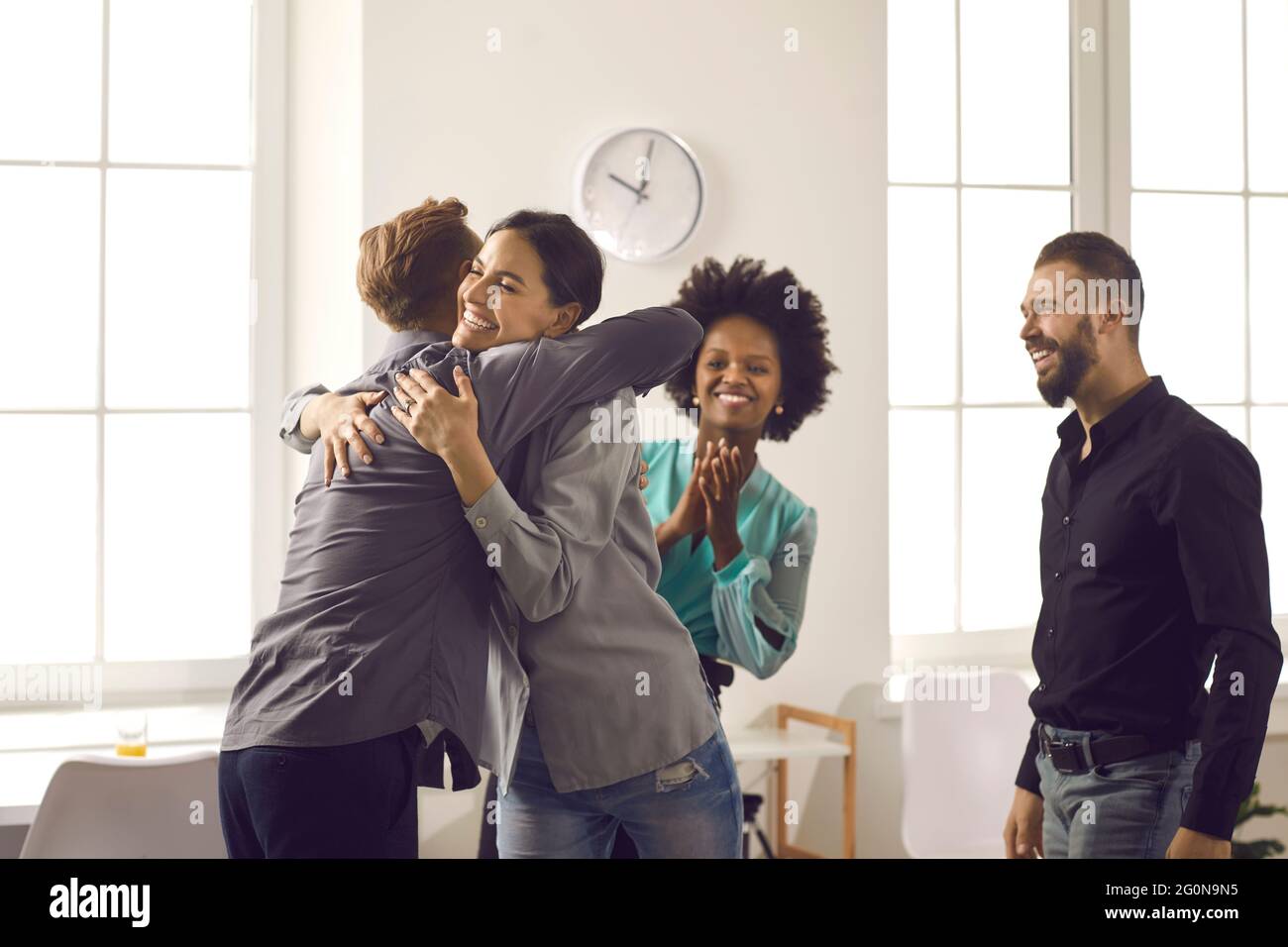 Group of colleagues hugging young man congratulating him on promotion ...