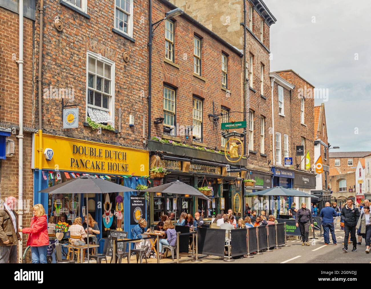 People sit at tables outside on a pavement eating and drinking. A pub ...