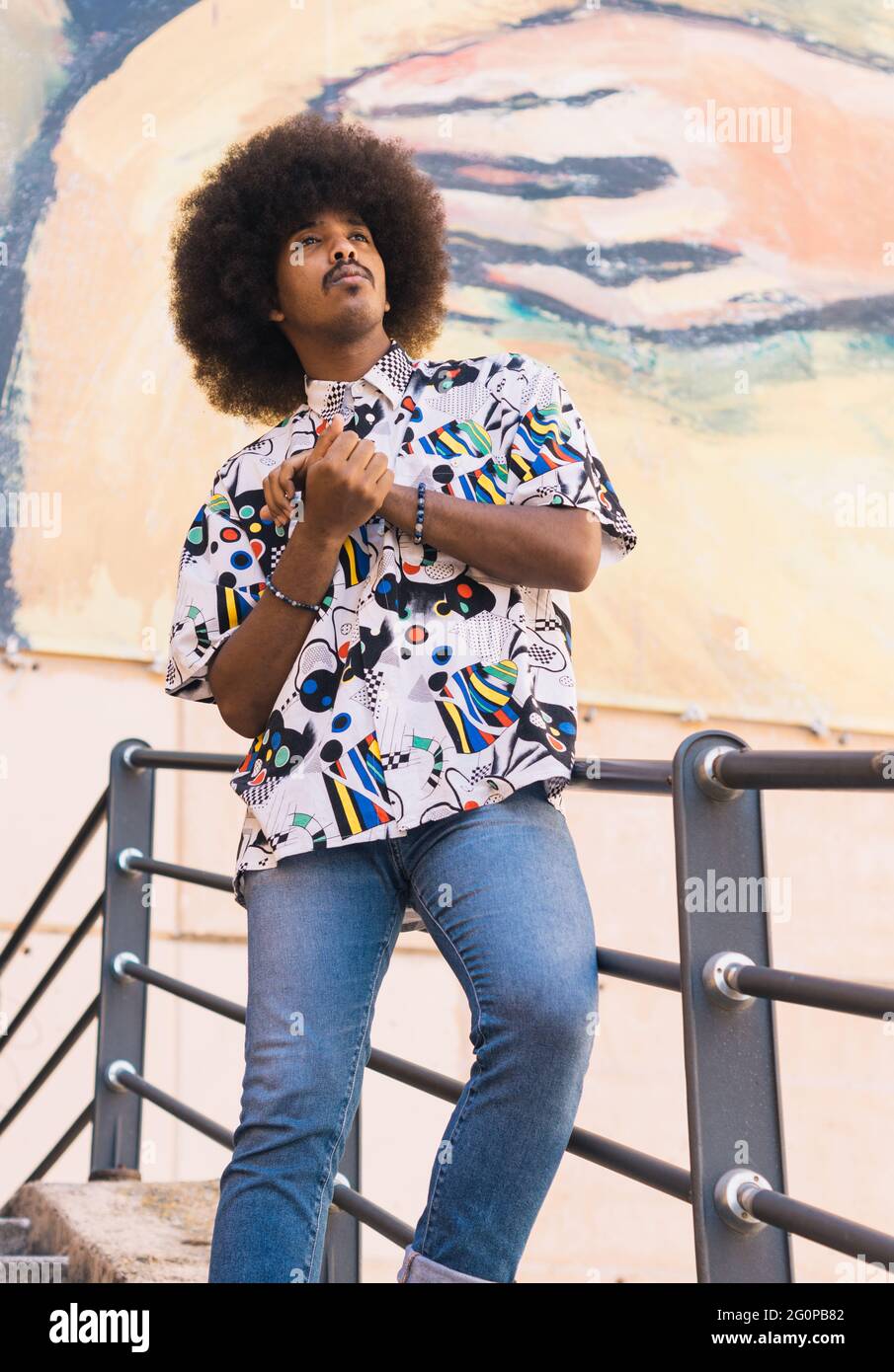 young black guy with afro hair standing leaning on a metal railing ...
