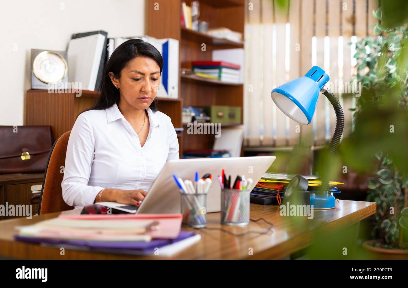 Latin american businesswoman sitting in office at workplace Stock Photo ...