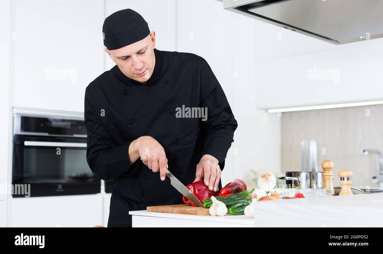 Professional chef in black uniform preparing vegetables on kitchen ...