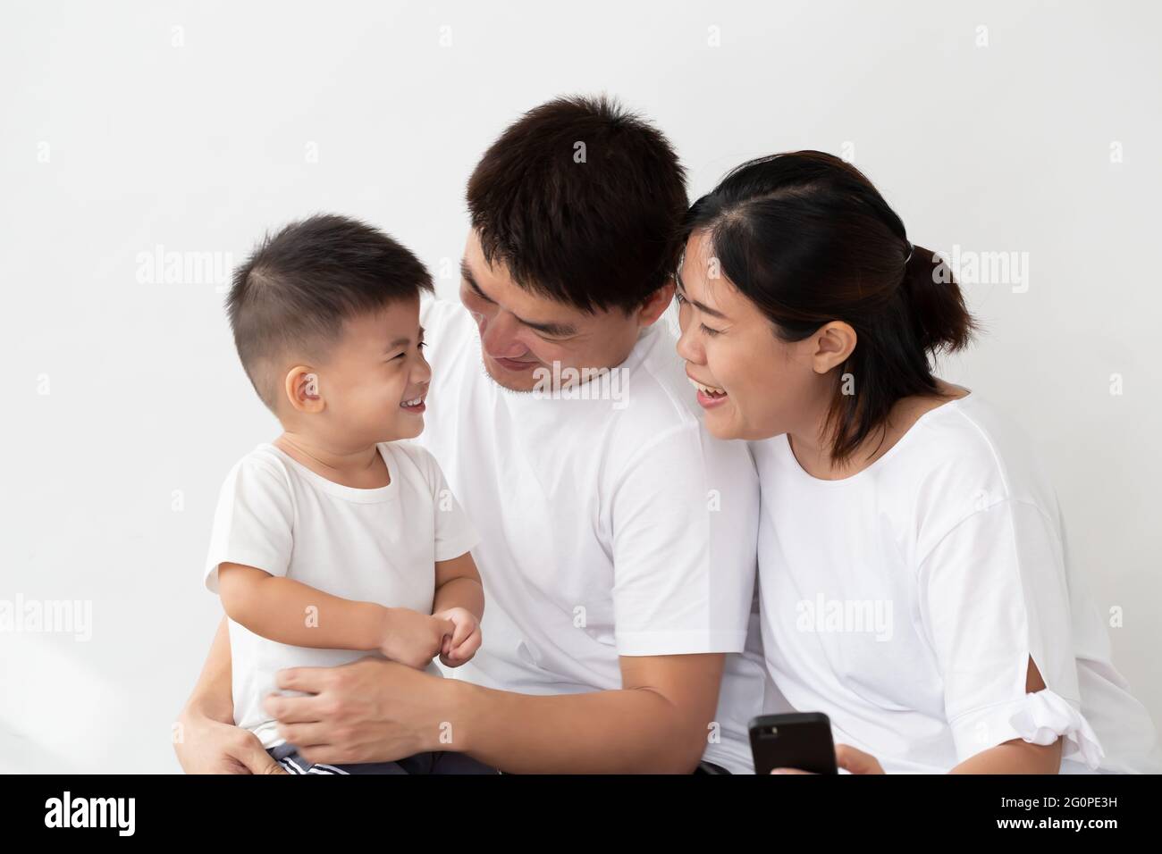 Happy young Asian family of three smiling and relaxing in white t ...