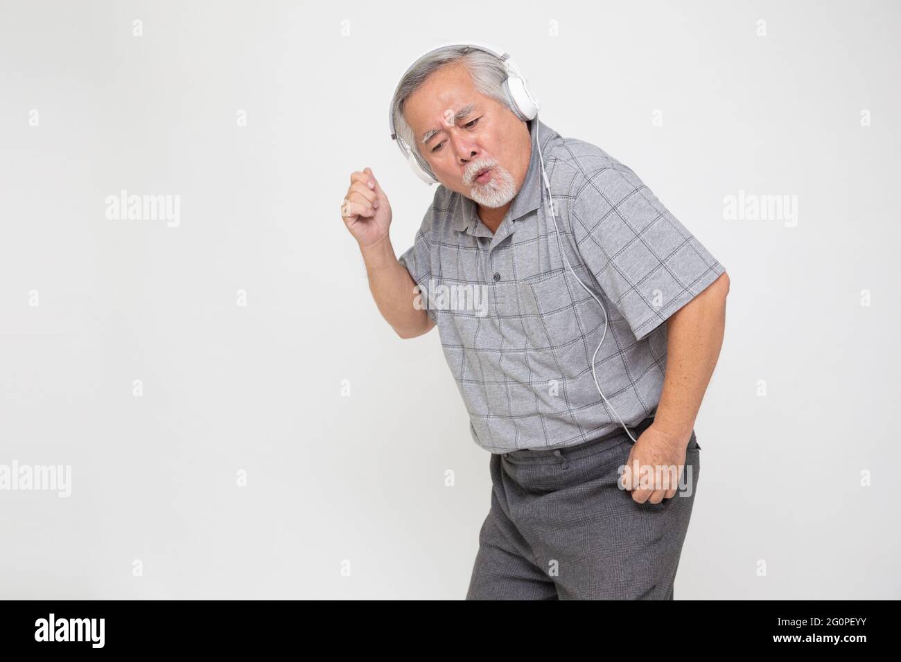 Senior Asian man listening music with headphones and dancing isolated ...