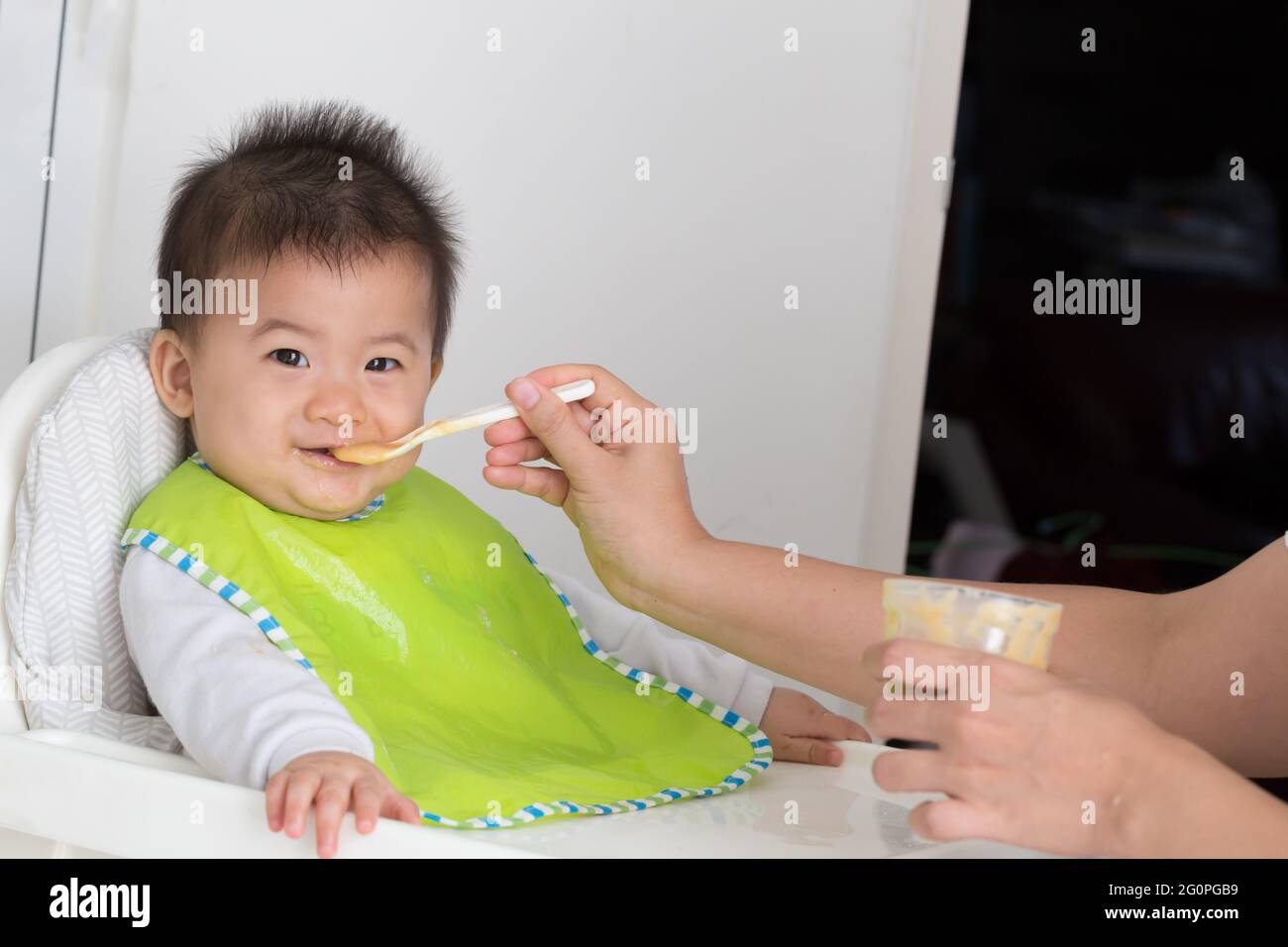 Happy baby child sitting in chair and mother feeding baby boy with ...