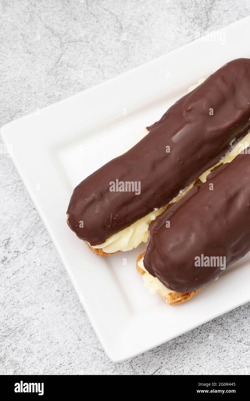 Chocolate eclair with a custard cream filling on a white plate. With a ...