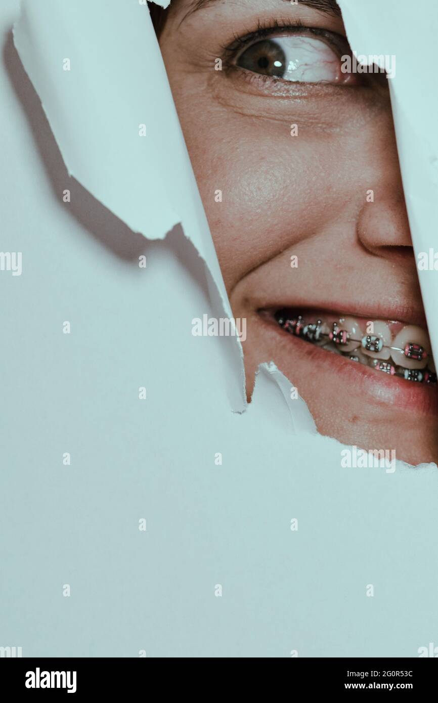 Vertical shot of a young Caucasian female smiling through a torn paper ...