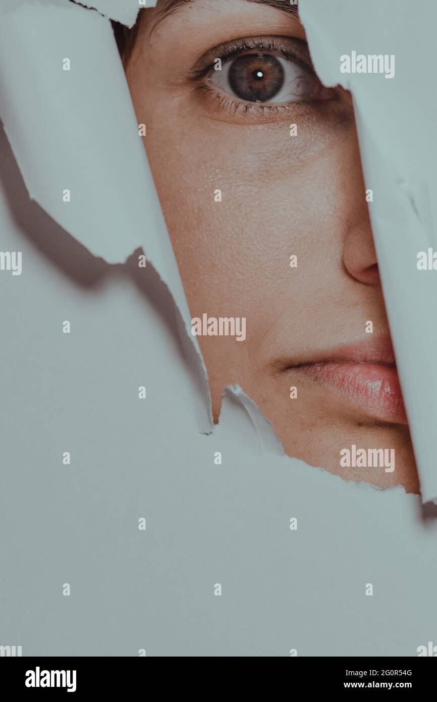 Vertical shot of a young Caucasian female face seen through a torn ...