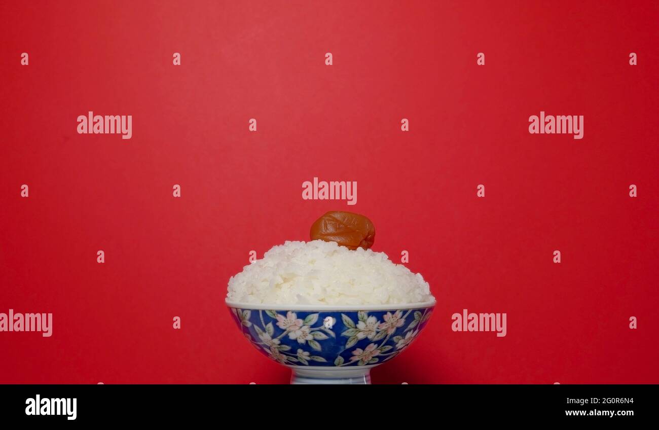 Bowl of rice with a japanese pickled ume fruit in front of red ...