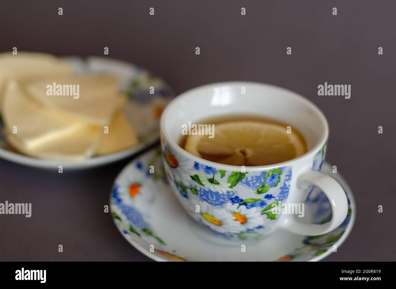 Cup of tea with lemon and Saucer with sliced cheese on gray background ...