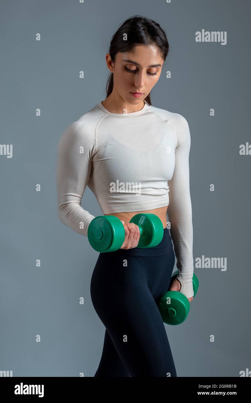 Sporty girl performing arm exercises with dumbbells on grey background ...