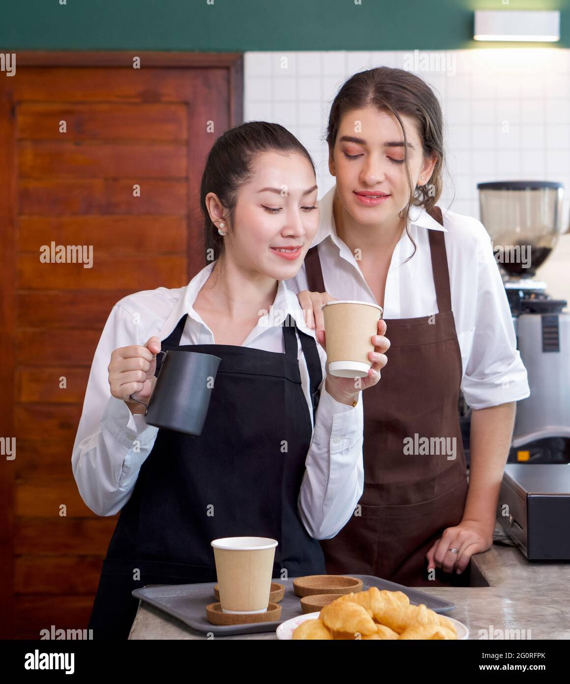 Young asian barista with a smile pouring milk from the jug into a paper ...
