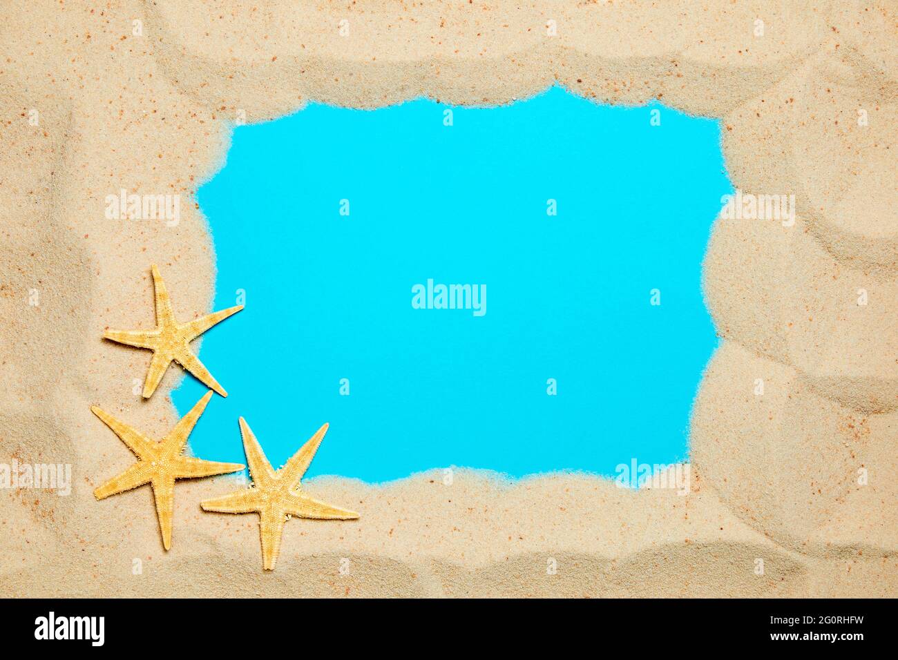 Summer background of sand decorated with starfish and blue copy space ...