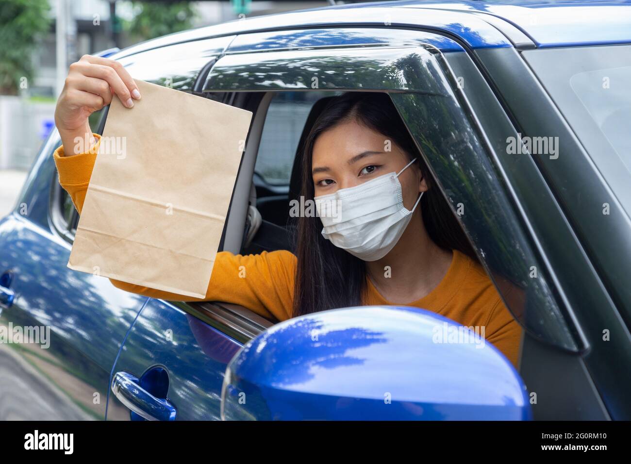 Asian woman wearing mask and holding paper bag of fast food through the ...