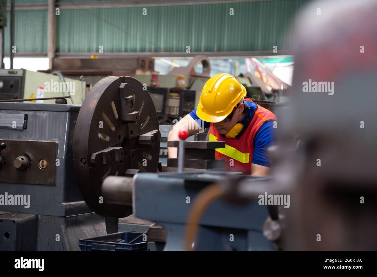 Asian mechanical engineer operating industrial lathe machine and ...