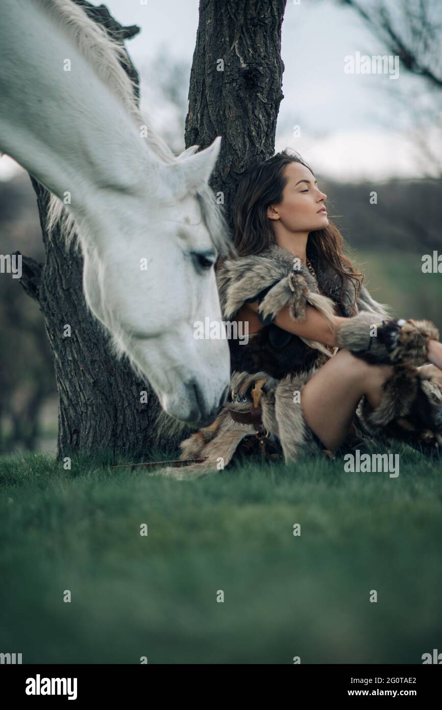 Woman in image of ancient warrior amazon sits and rests under tree in ...