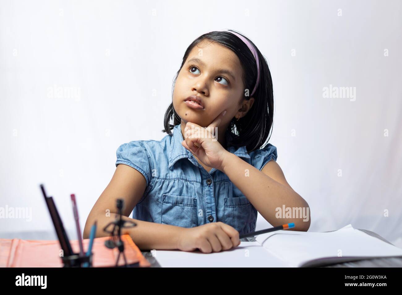 A pretty Indian girl child thinking and looking upward while studying ...