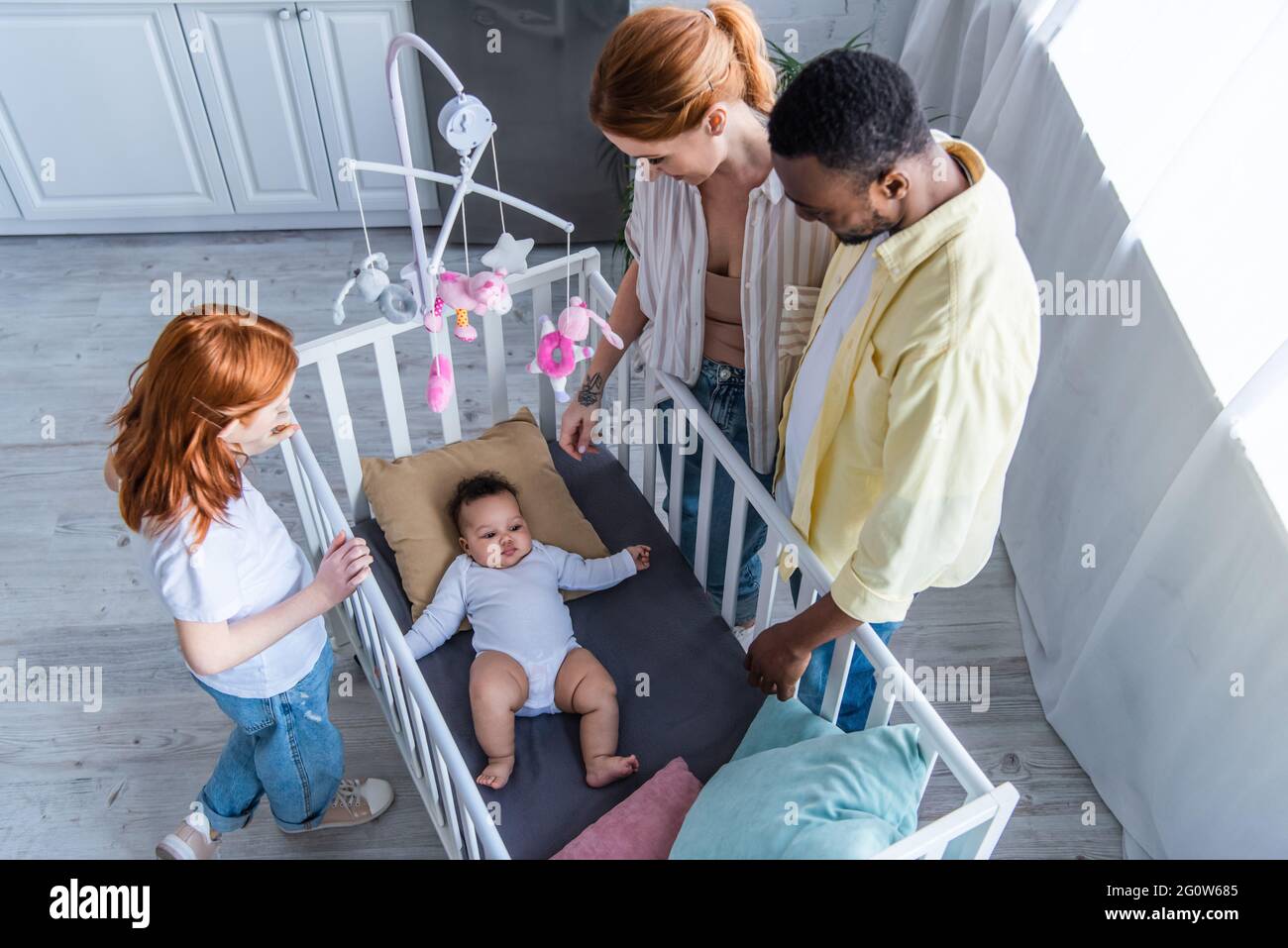 overhead view of multiethnic family looking at infant girl lying in ...