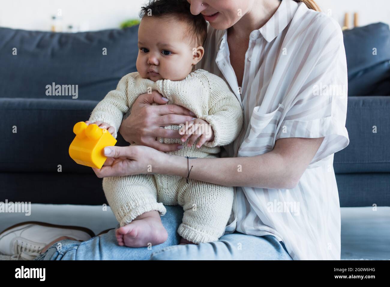 woman holding building block while playing with infant african american ...