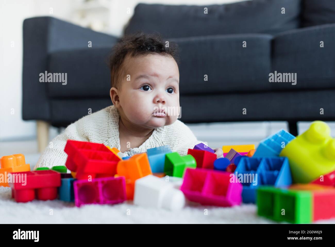 african american baby girl crawling on floor near blurred colorful ...