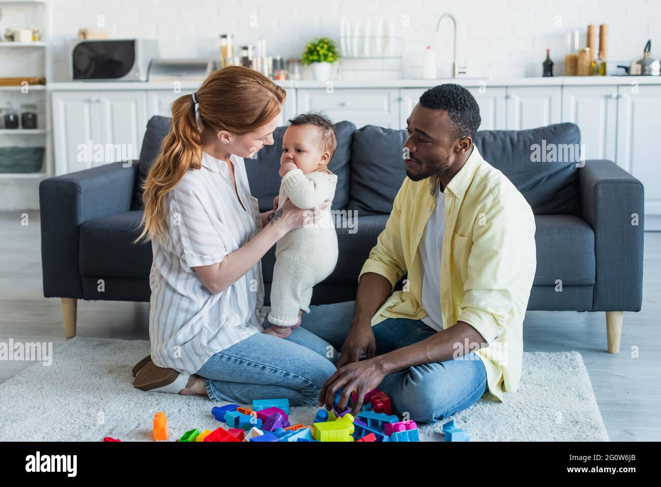 mother holding infant daughter while sitting on floor near african ...