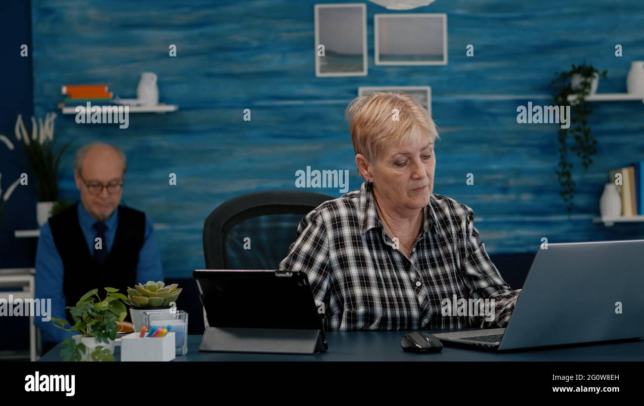 Multitasking retired woman reading on laptop and tablet in same time ...