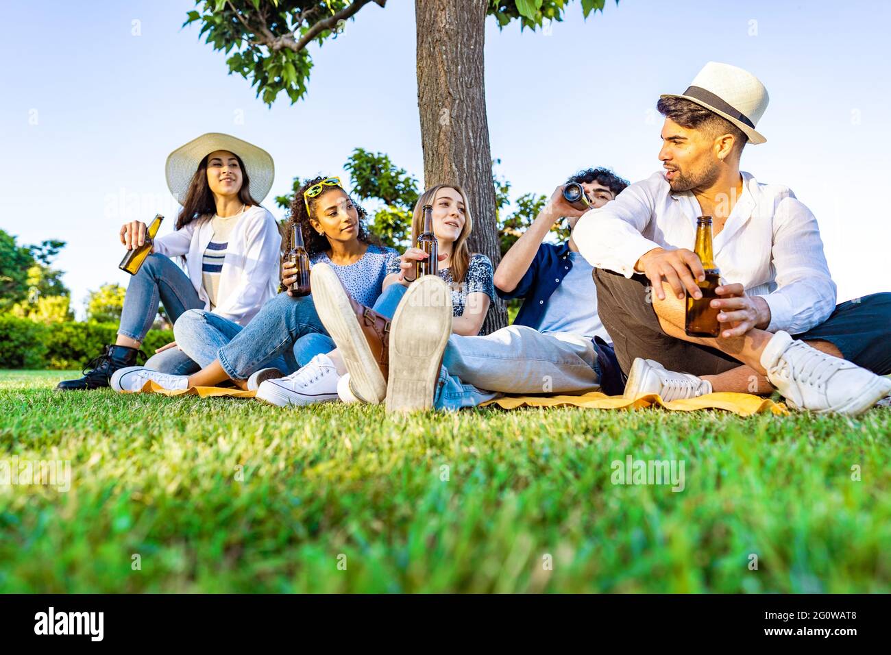 Group of five happy young diverse multiracial gen z people in outdoor party drinking beer from ...