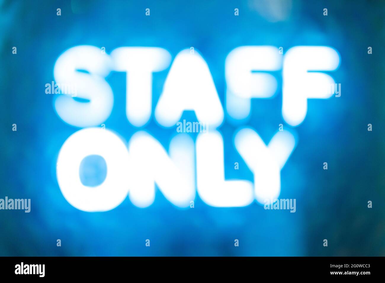 Blurred neon letters, signboard staff only on a black wall close-up ...