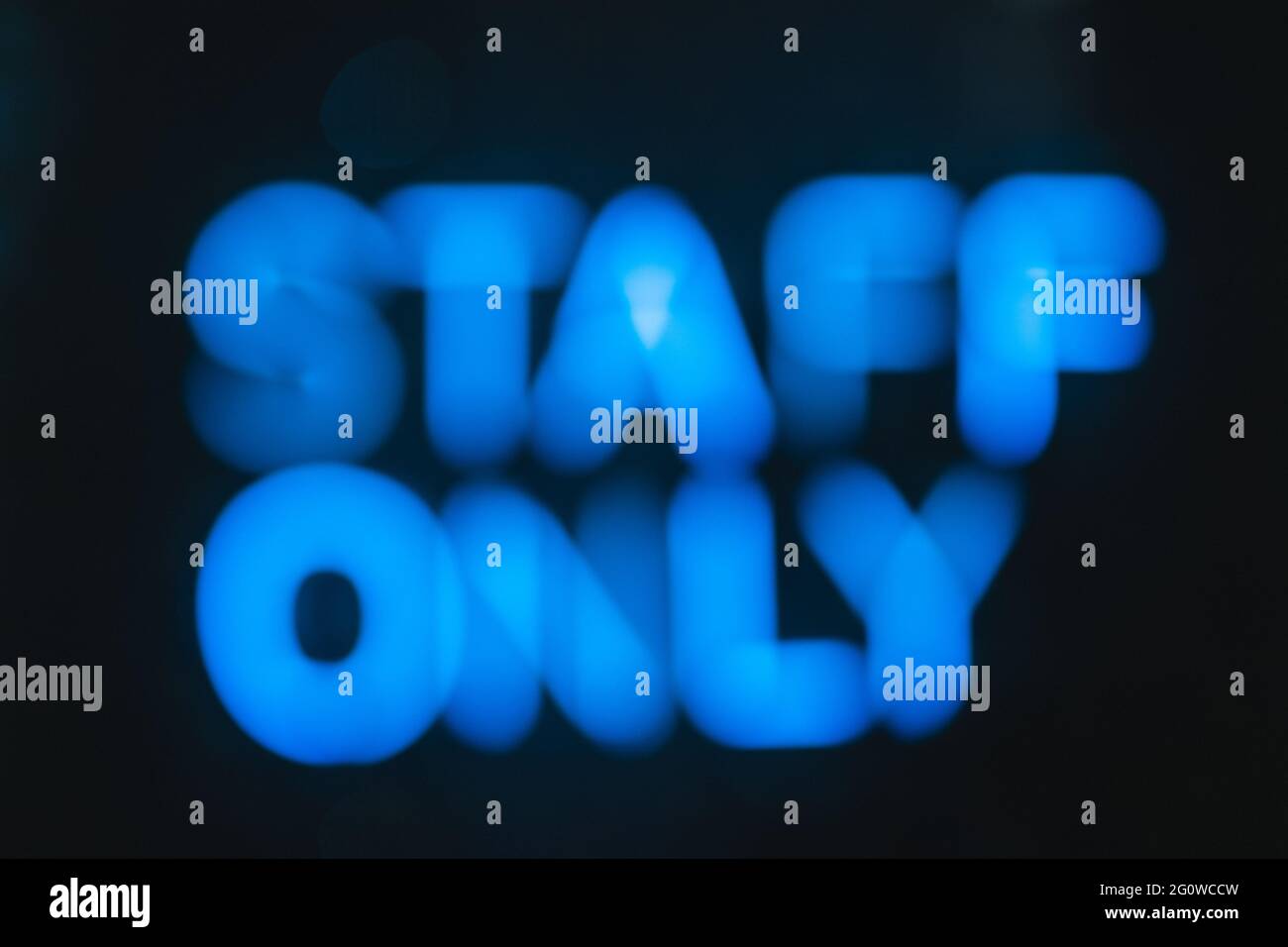 Blurred neon letters, signboard staff only on a black wall close-up ...