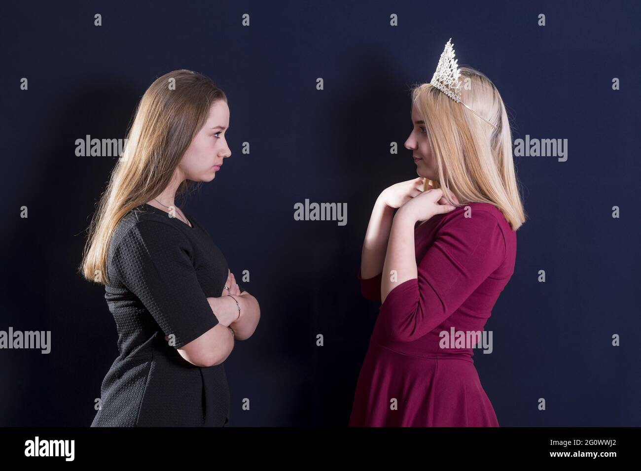 Two young girls stand against each other. They look in the eyes. One is ...