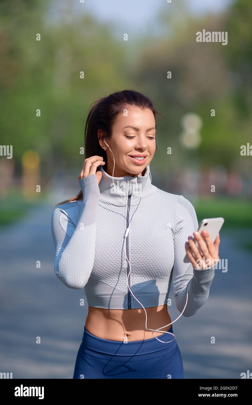 Vertical photo - a young woman jogging. She sets up the music on her ...
