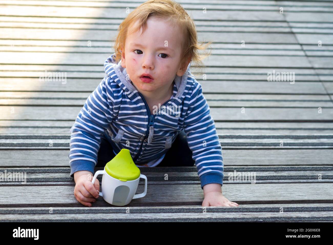 Young toddler with scratched and dirty face crawling up wooden stairs ...