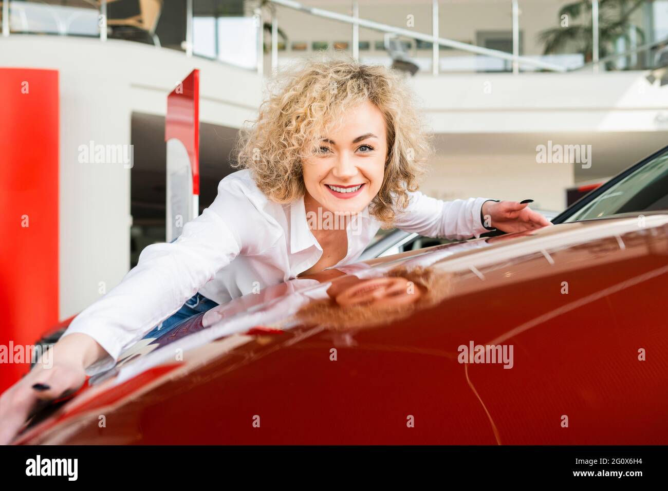 Beautiful woman hugging her new car in dealership. Happy girl rejoices ...