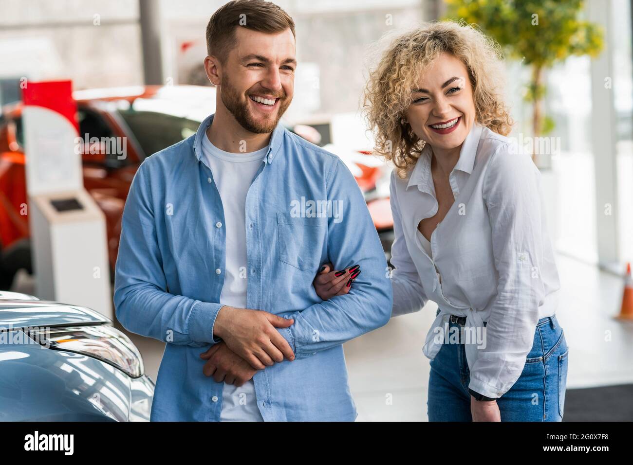 Young couple walks through the car dealership in search of a new car ...