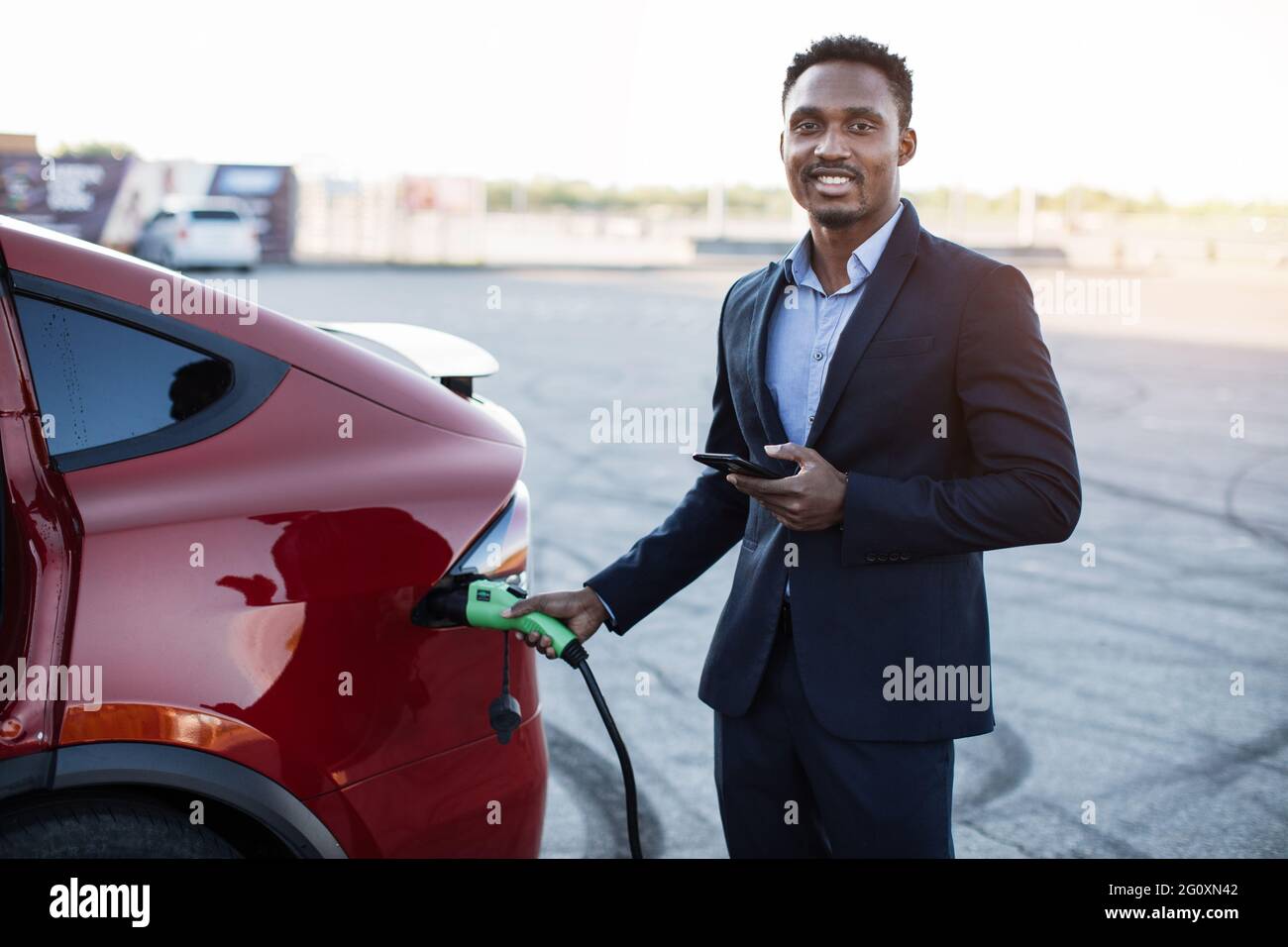 Young successful businessman charging electric car on station and using ...