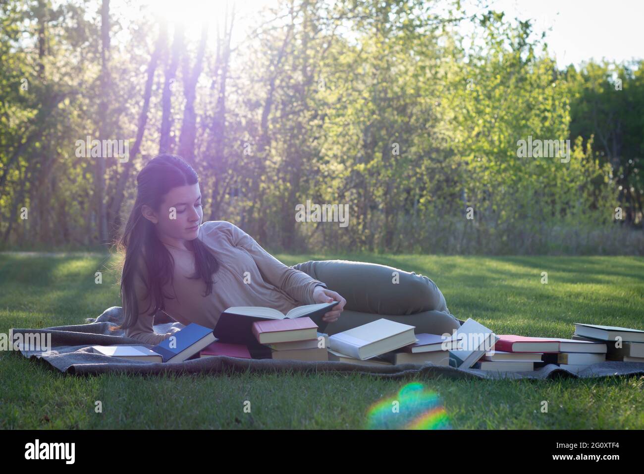 Teen girl, young woman relaxing on blanket outside reading a book ...