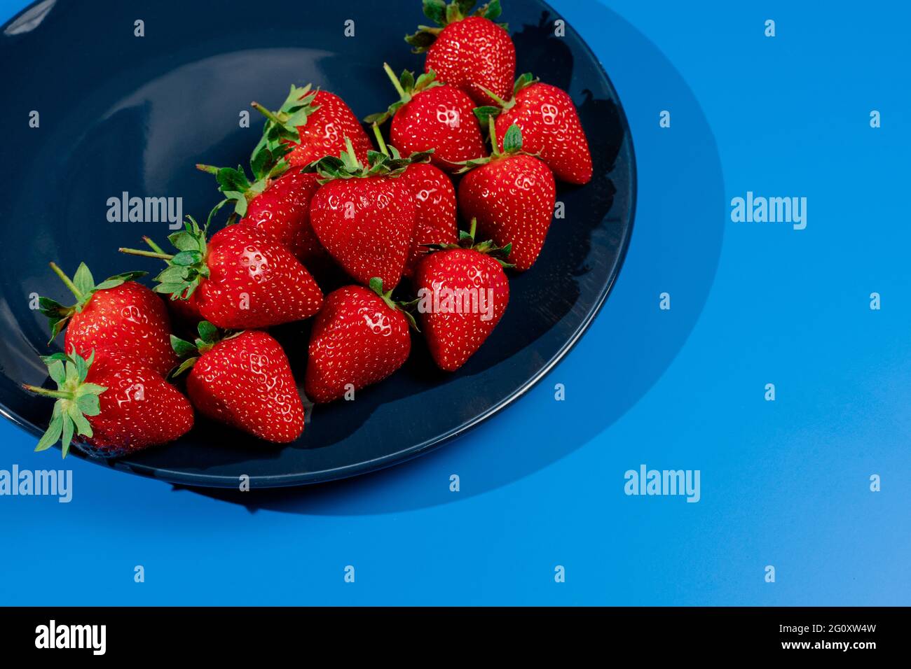 Bunch of strawberry on plate on blue background. Summer seasonal red ...