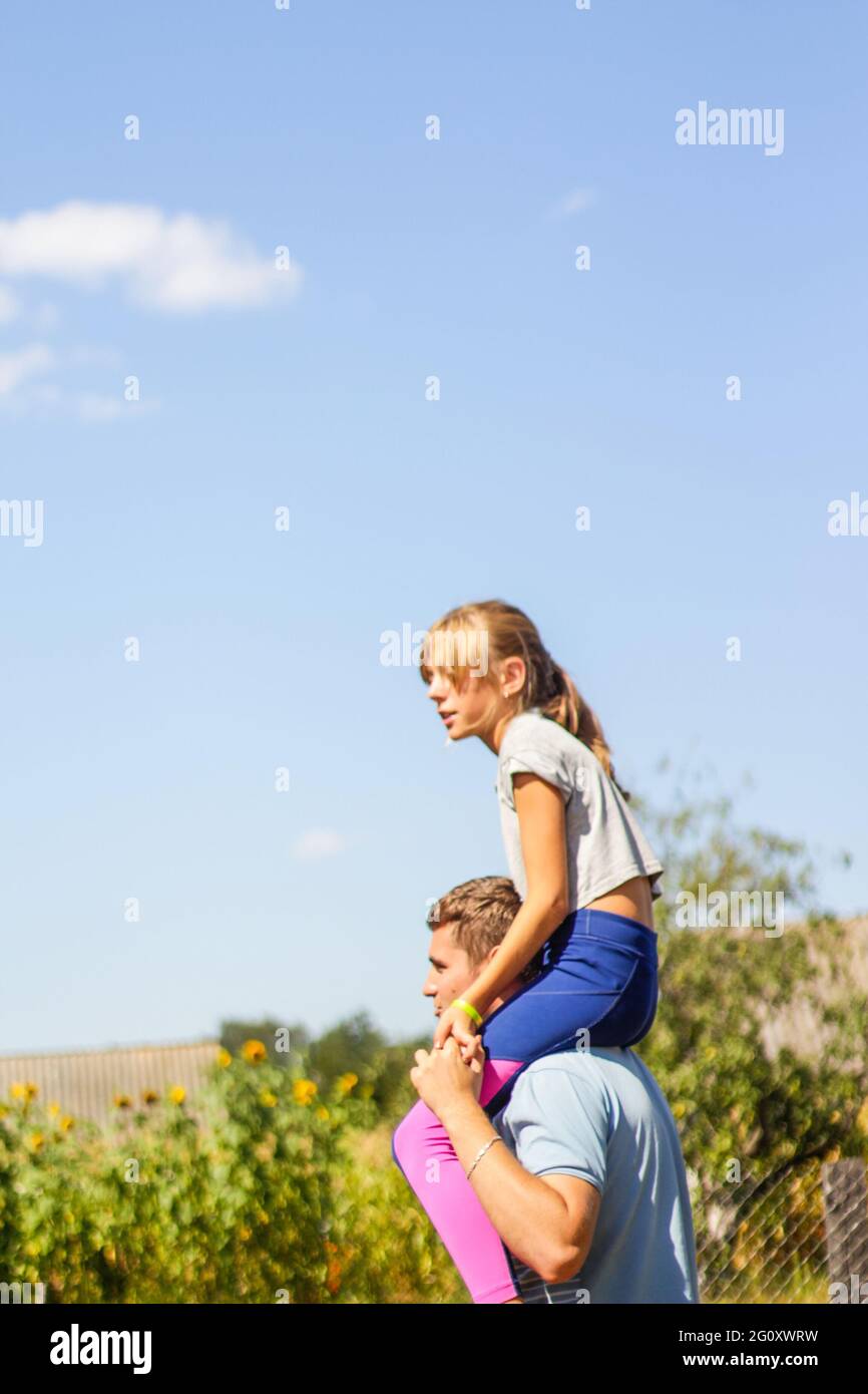 Defocused brother riding sister on back. Portrait of happy girl on man shoulders, piggyback ...